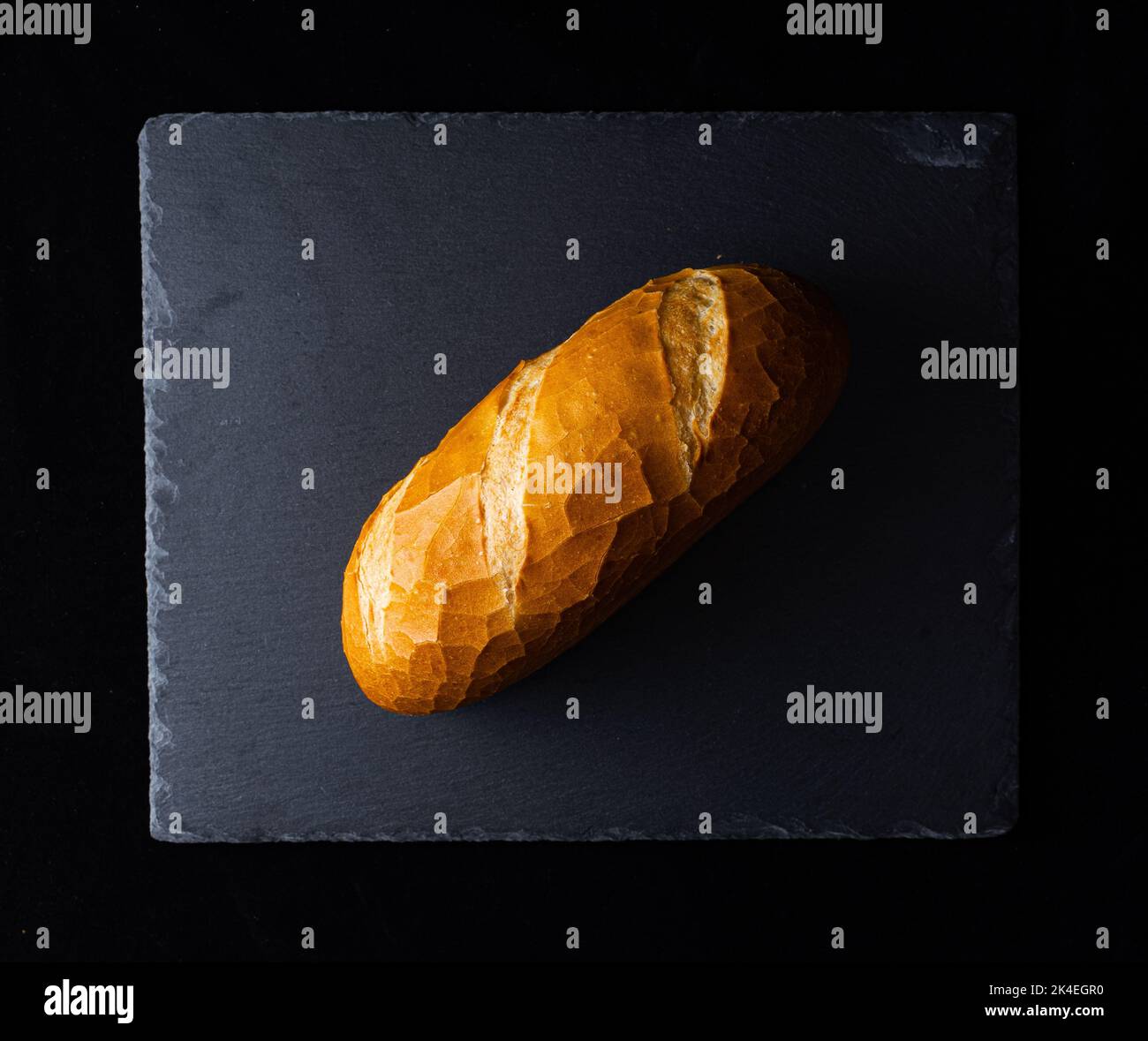 A top view of a french loaf bread served on a slate with a black ...