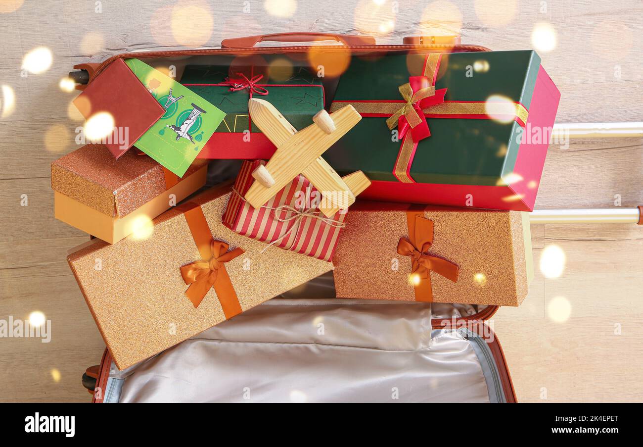 Open suitcase with gift boxes and wooden airplane on floor. Christmas ...