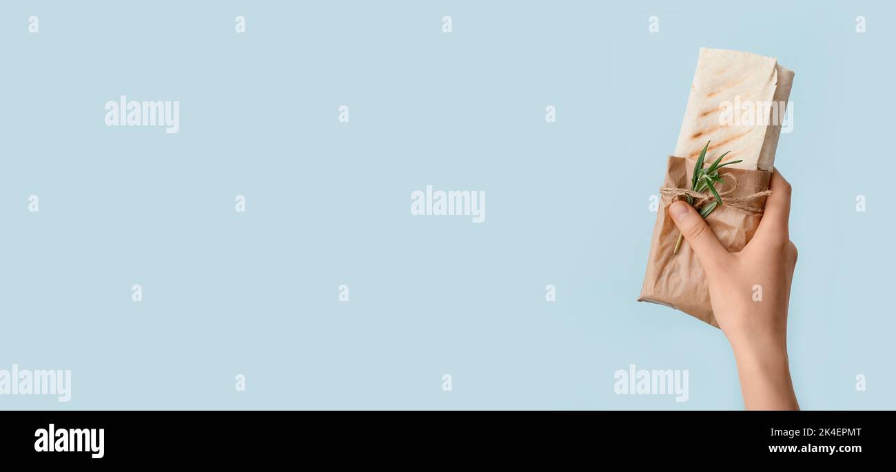 Female hand holding tasty doner kebab on light blue background with ...