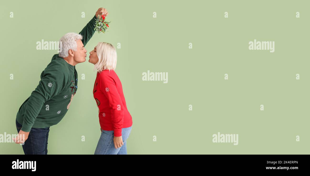 Mature couple kissing under mistletoe branch on color background with ...