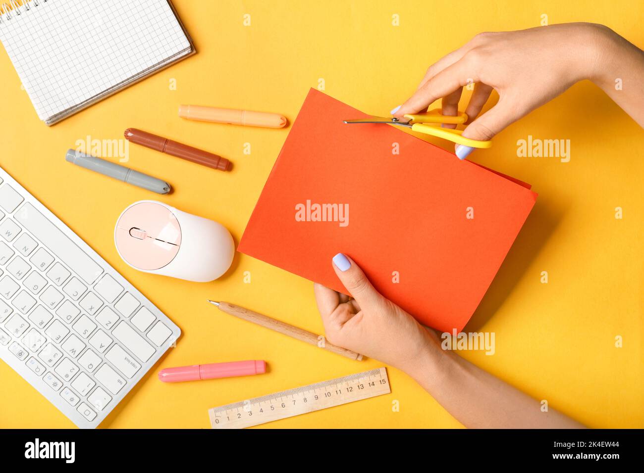 Woman cutting color paper with scissors, keyboard, computer mouse and ...