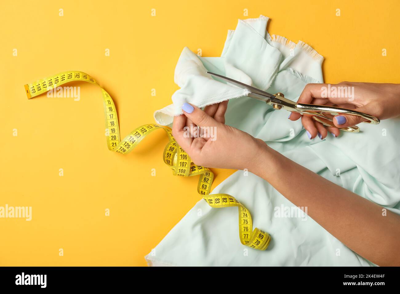 Female tailor cutting fabric with scissors on color background Stock ...