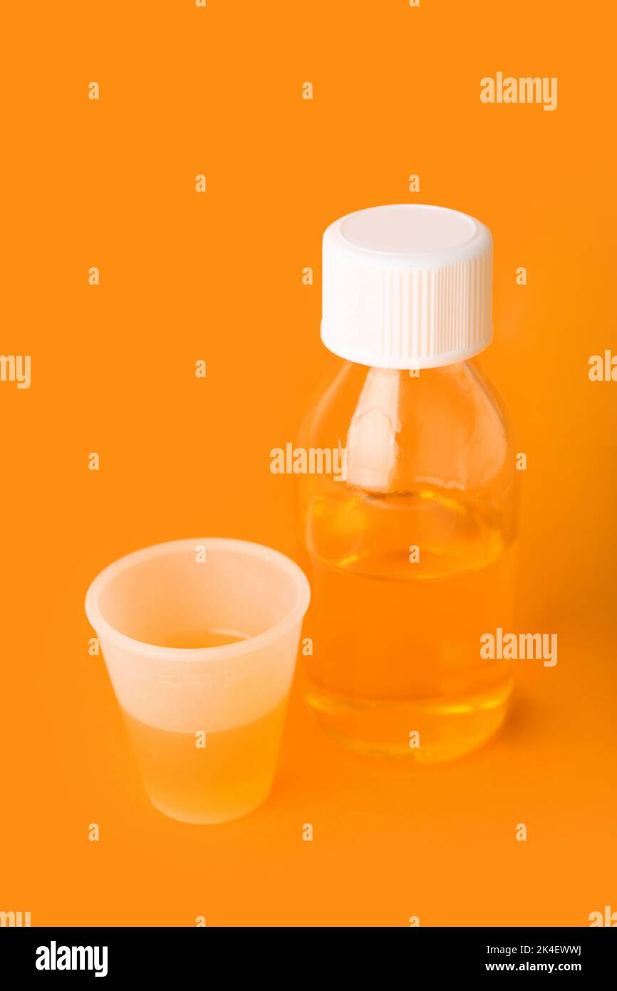 Bottle of cough syrup and cup on orange background Stock Photo - Alamy