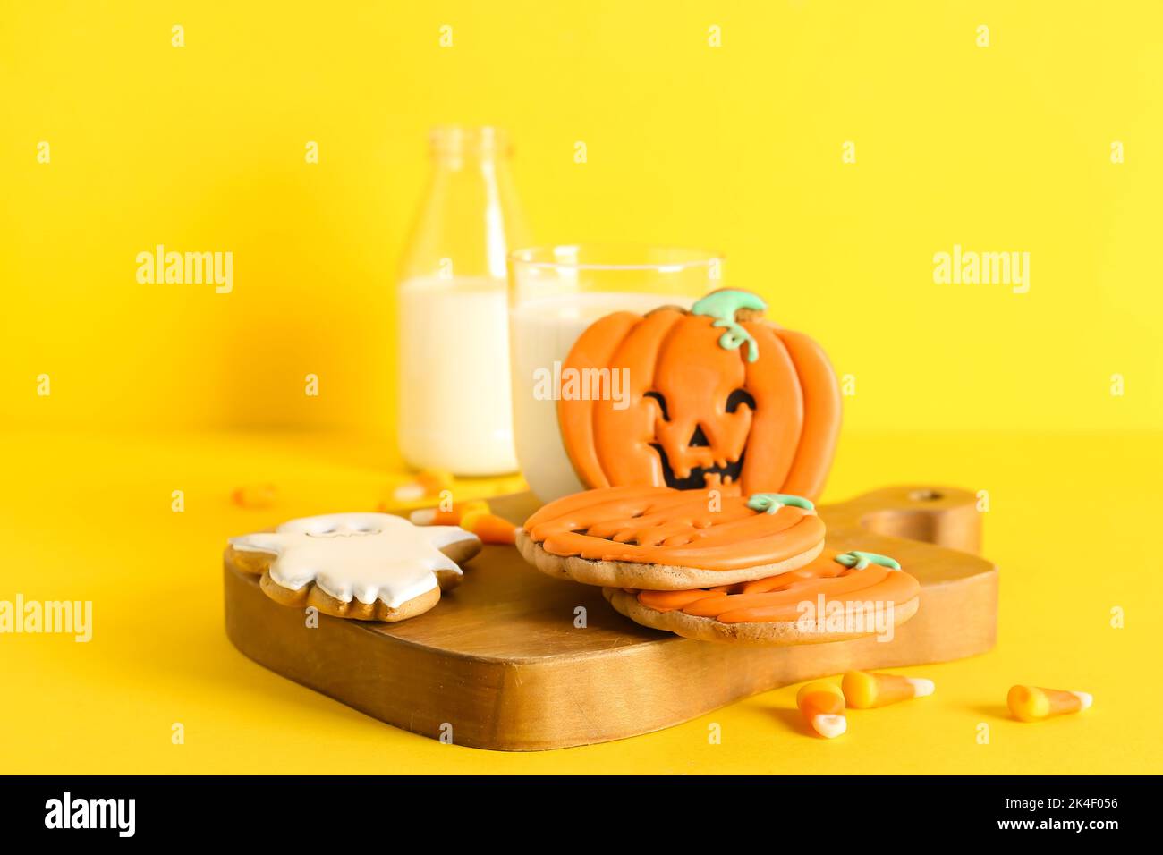 Board with Halloween cookies, candy corns and glass of milk on yellow ...