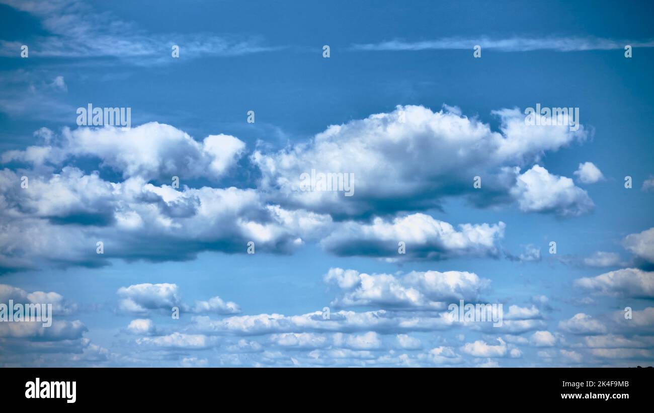 A scenic view of white puffy clouds floating in the blue sky background ...