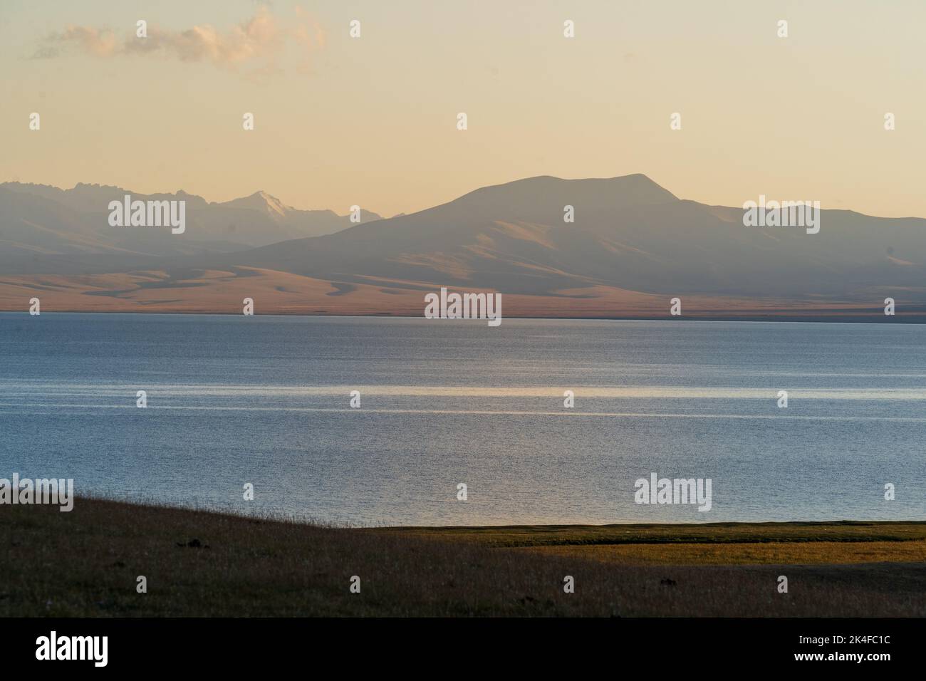 Shore of Song Kul Lake and surrounding mountains at golden hour sunset ...