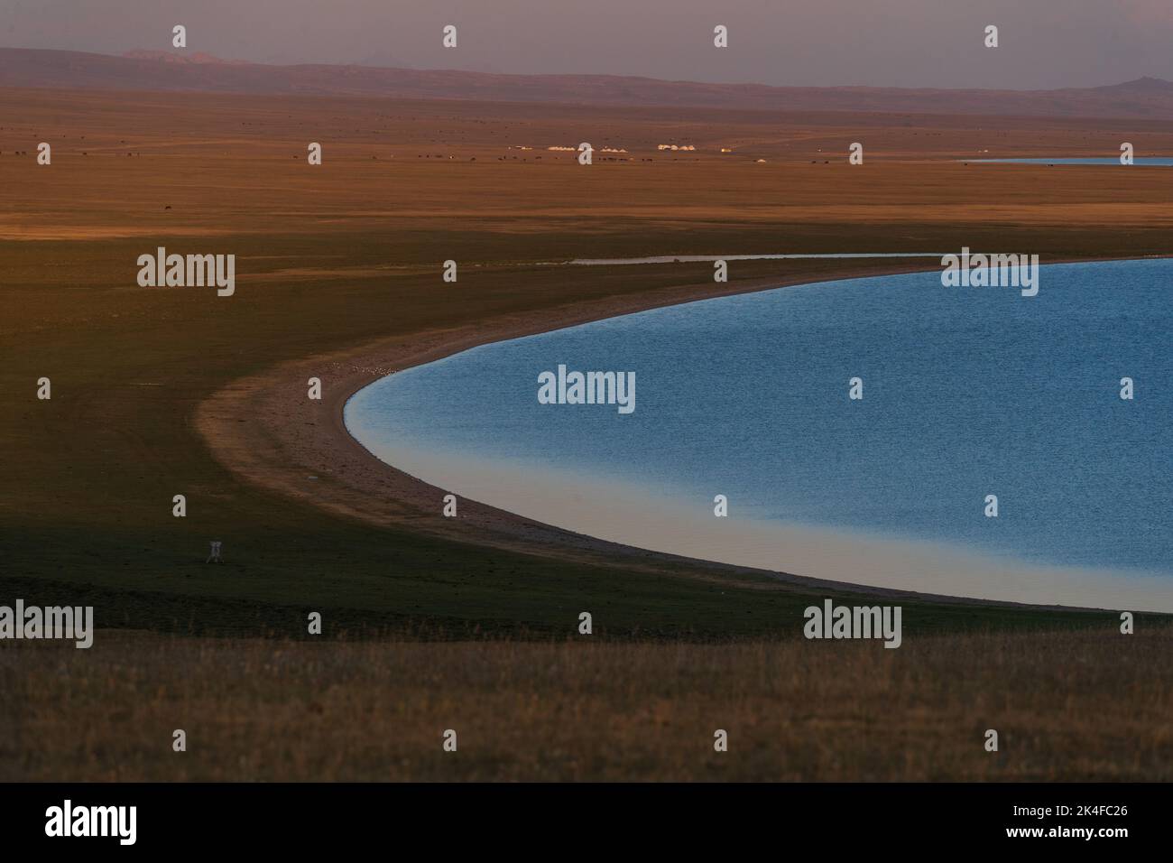 Shore of Song Kul Lake and surrounding mountains at golden hour sunset ...