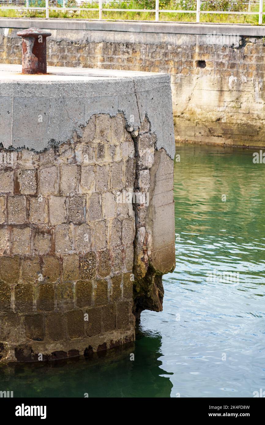 Old destroyed cracked stone wall of a sea quay with a rusty bollard ...