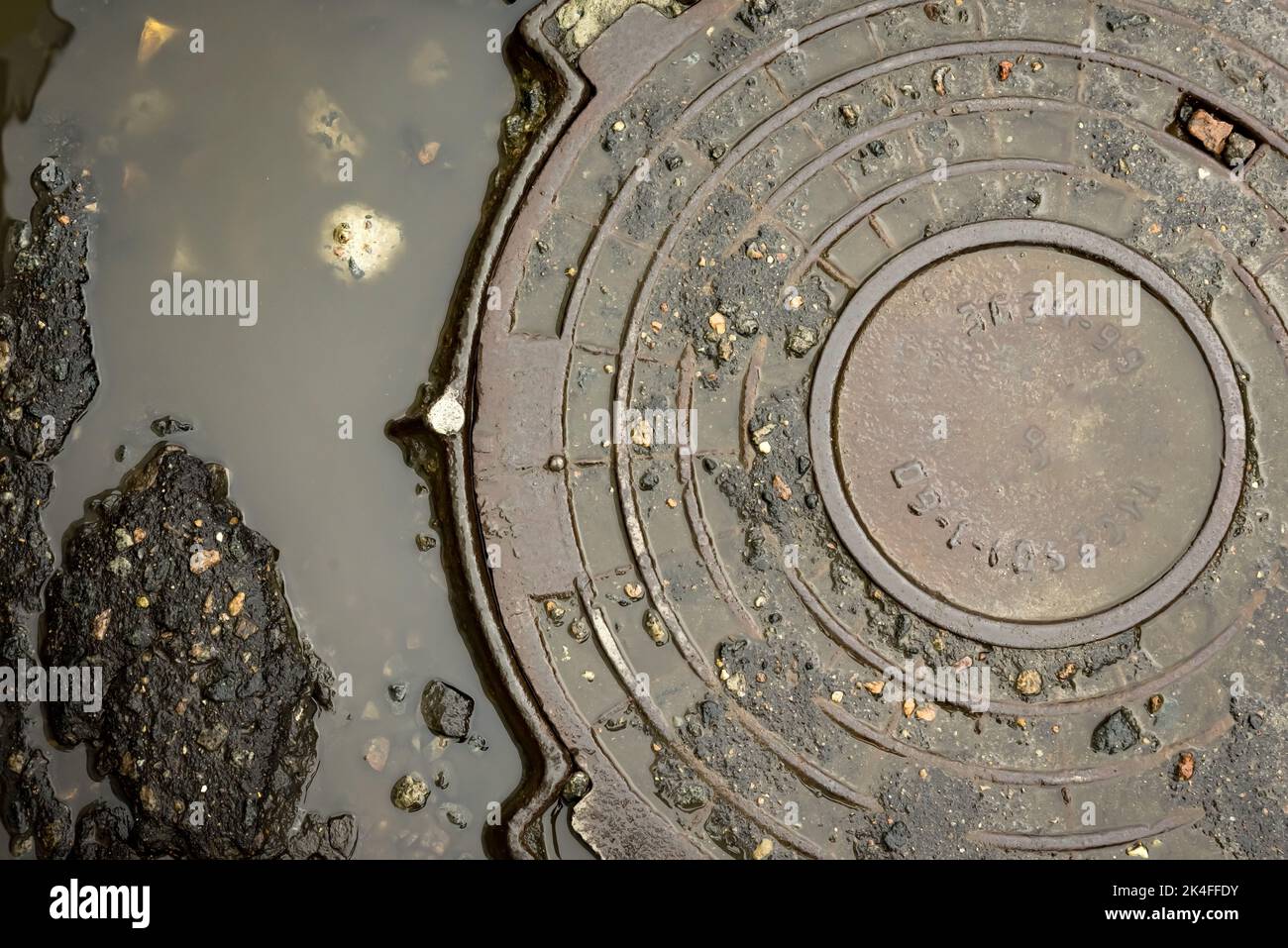 Sewer manhole in the water on the road. Manhole on a destroyed asphalt ...