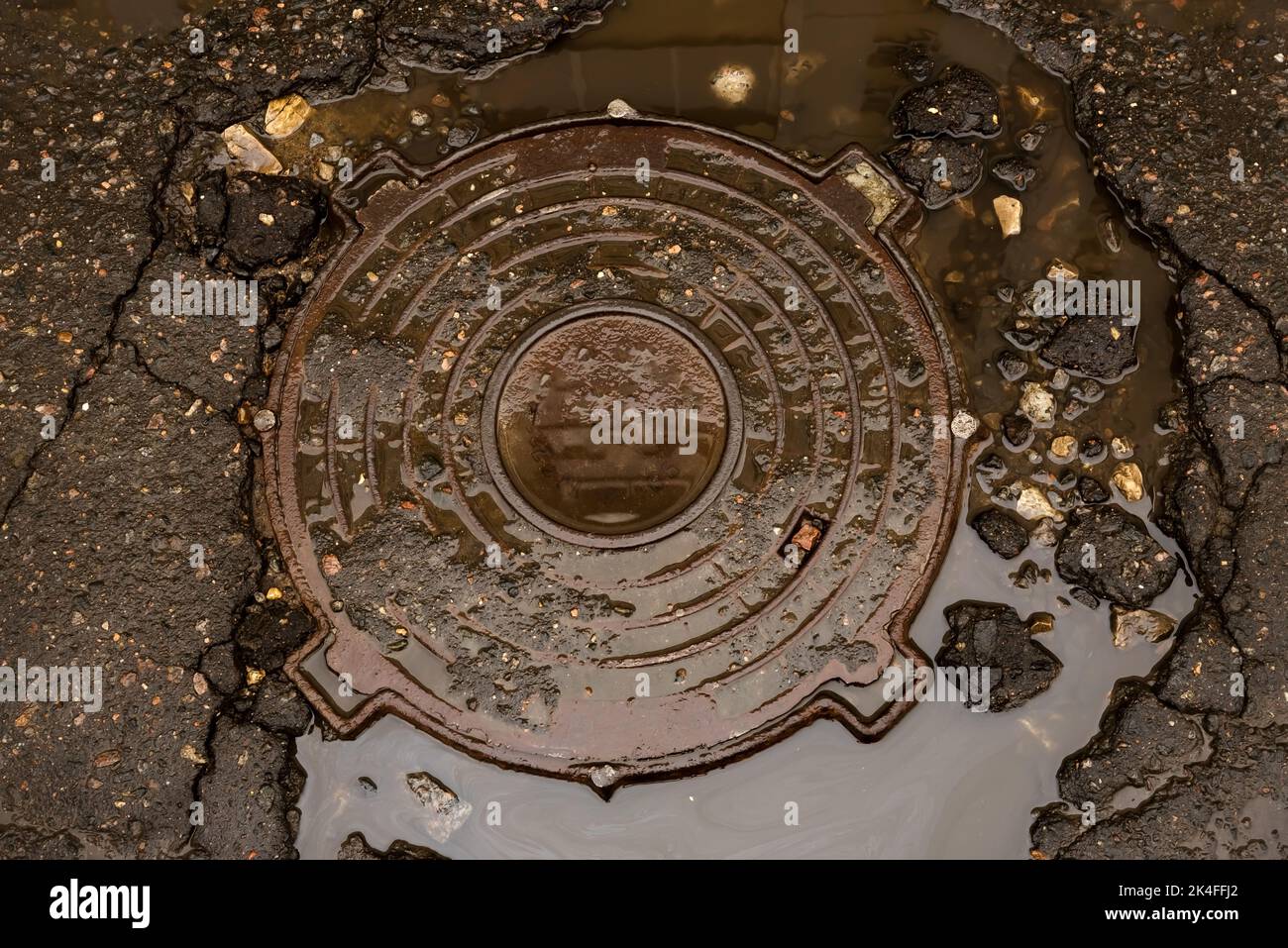 Sewer manhole in the water on the road. Manhole on a destroyed asphalt ...