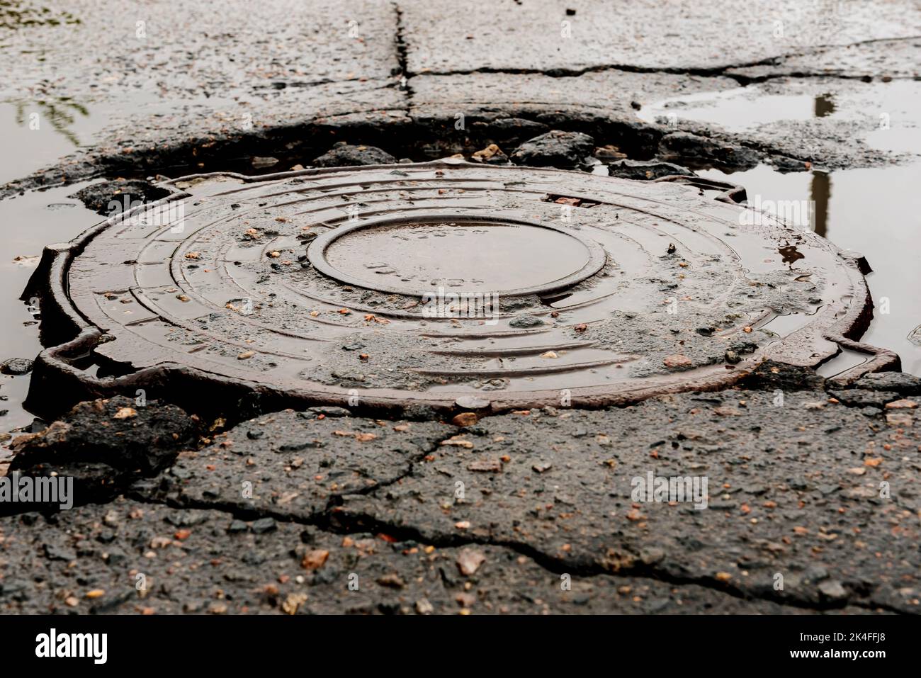 Sewer manhole in the water on the road. Manhole on a destroyed asphalt ...