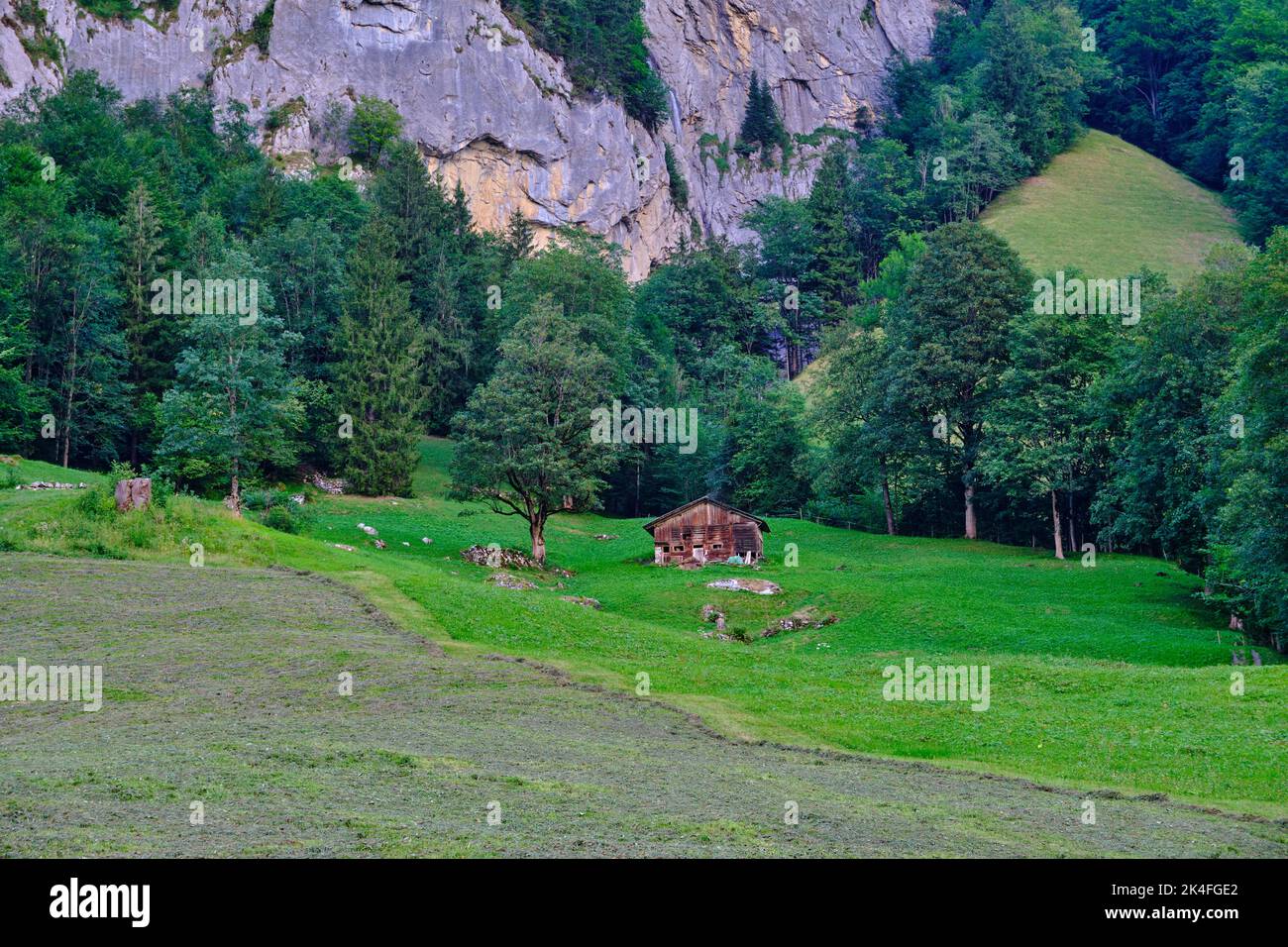 A wooden barn in the middle of the field surrounded by mountains in ...