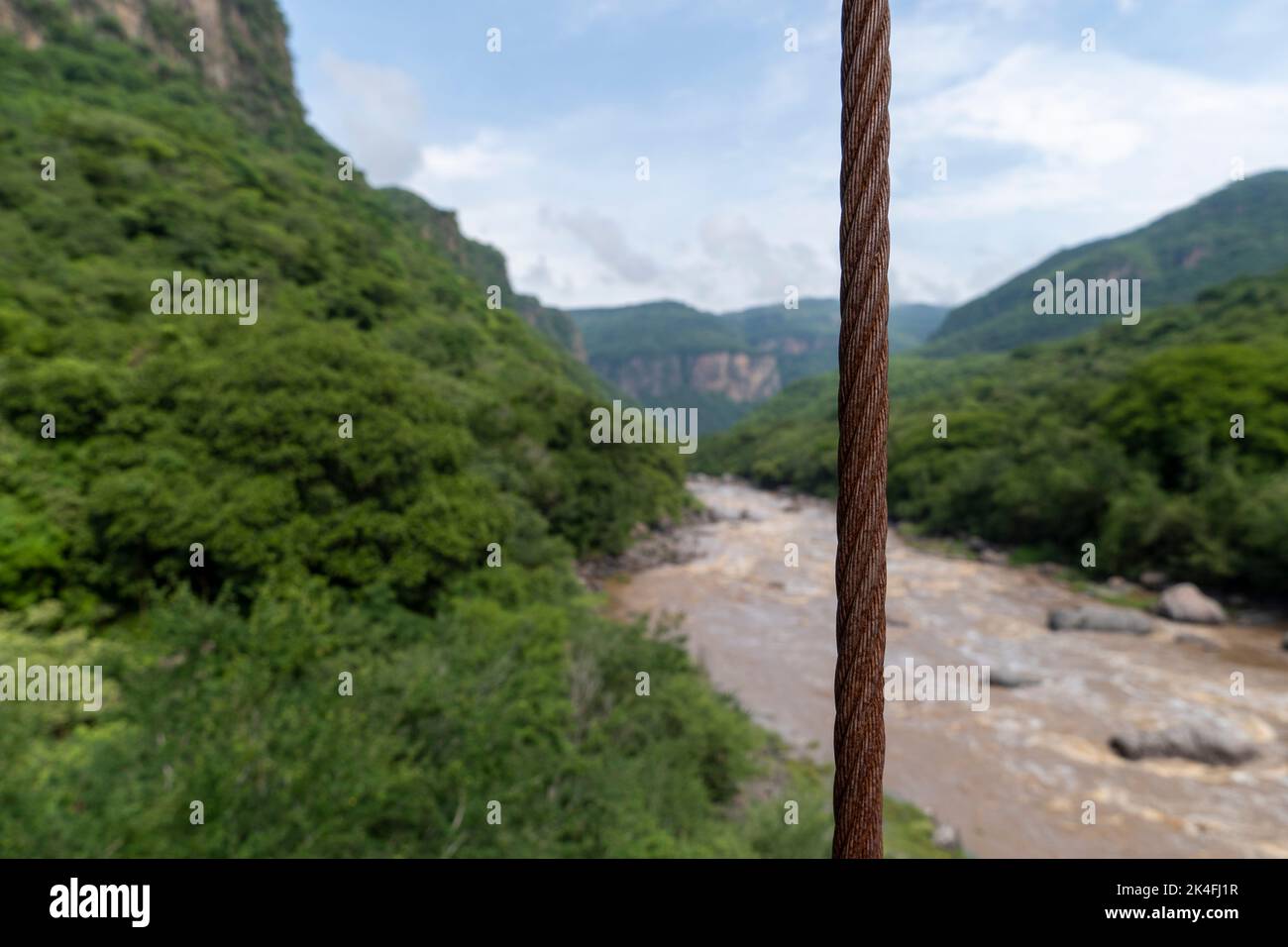 rusty cable, river and mountain in the background, vegetation barranca ...