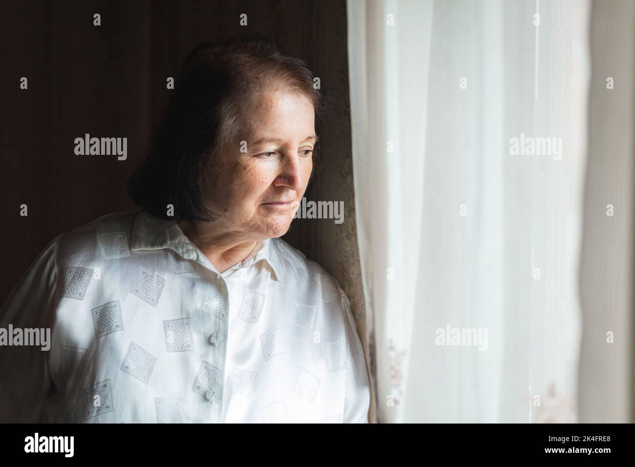 Elderly woman standing and looking through the window Stock Photo - Alamy