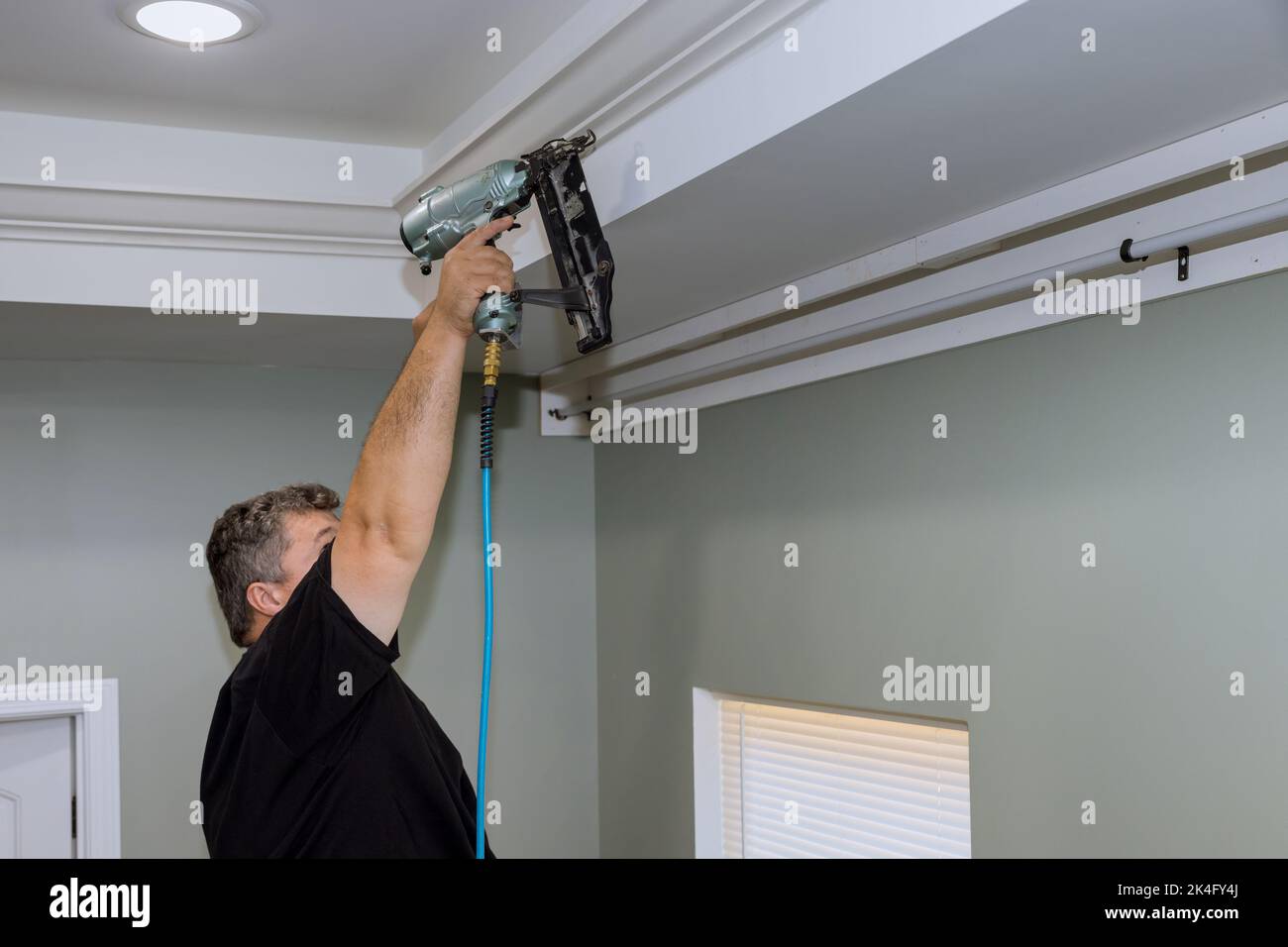 An experienced carpenter is seen in nailing wooden crown molding ...