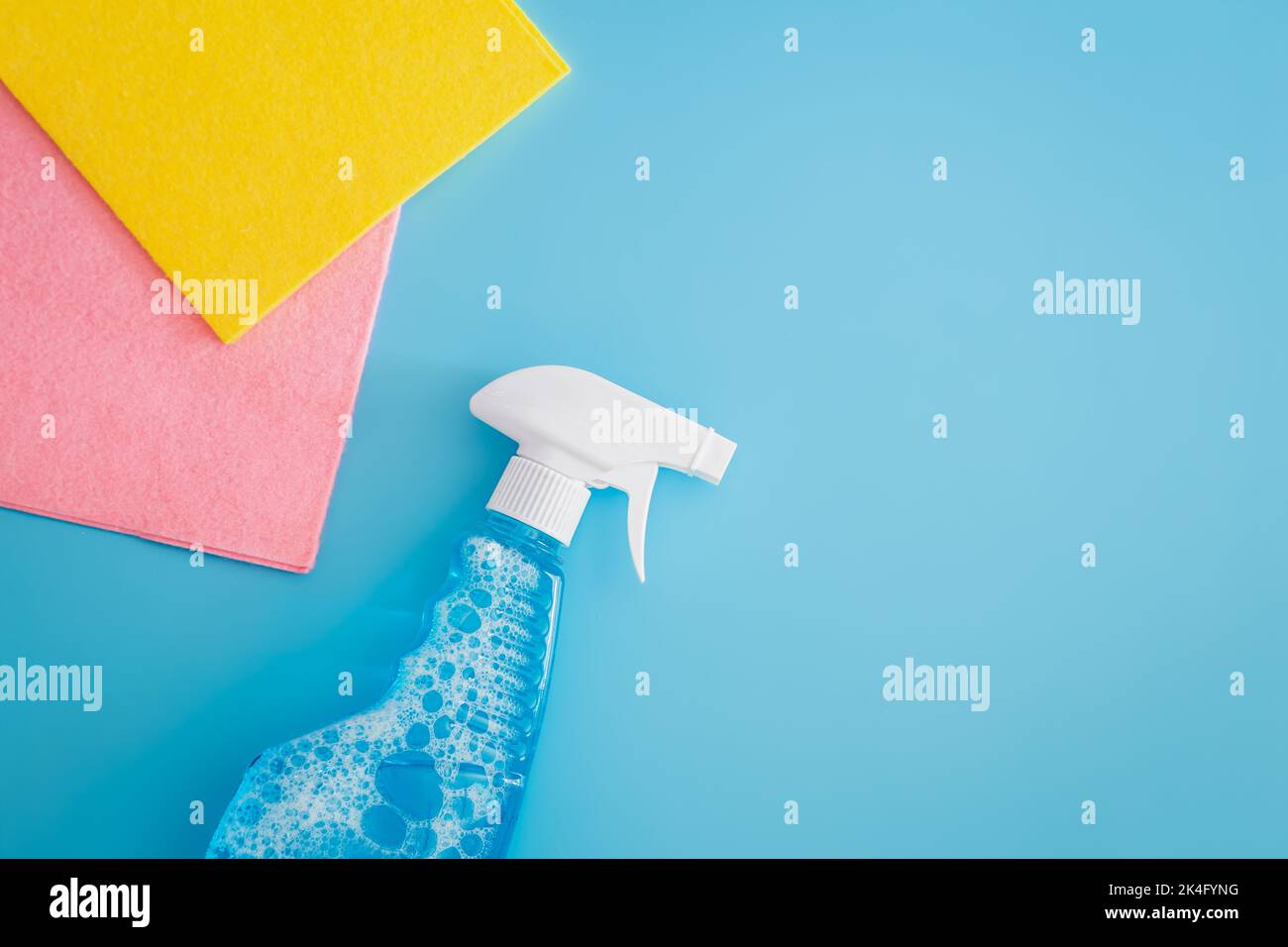 Blank cleaning spray bottle and colored rags on blue background, flat ...