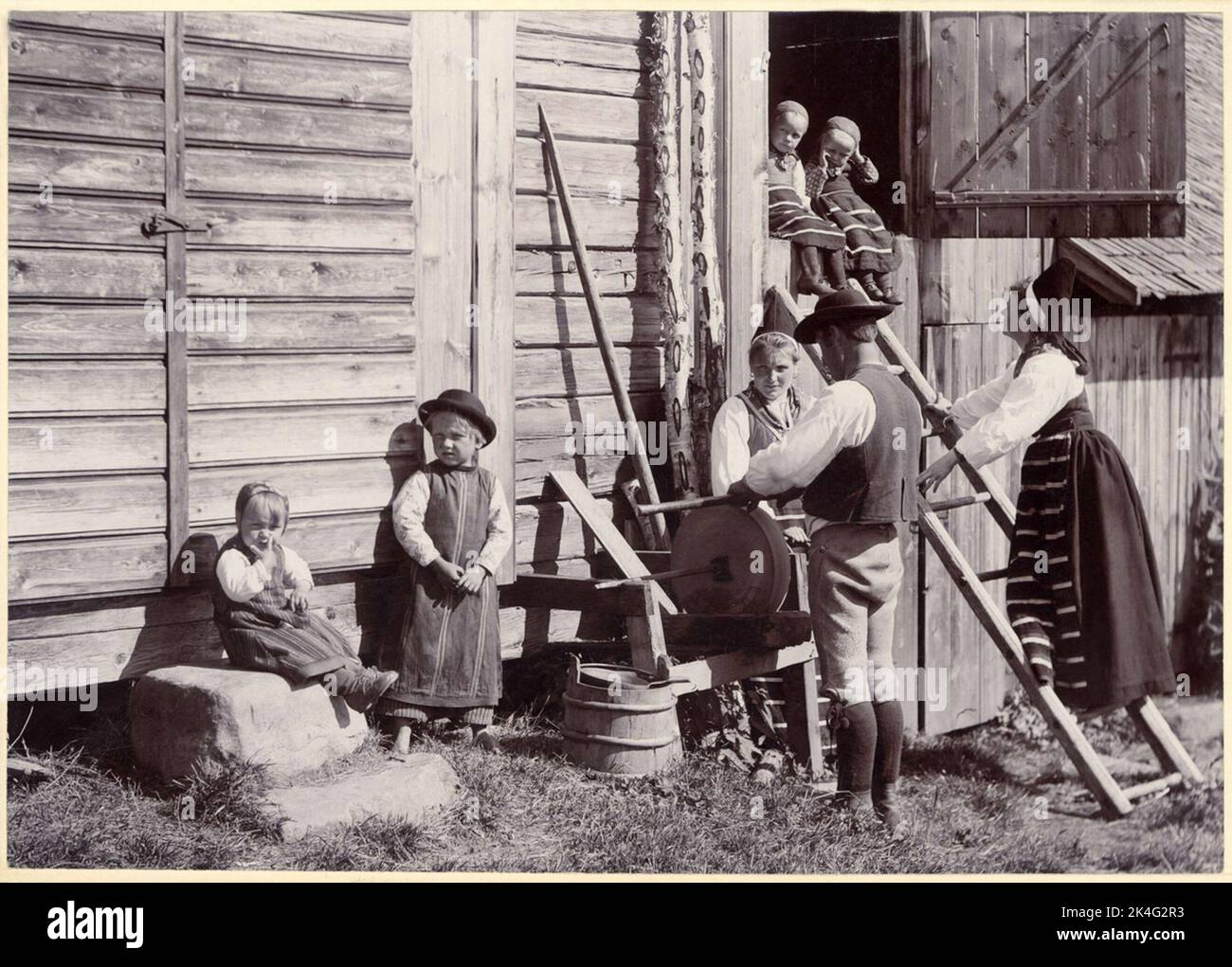 A family dressed in folk costume outside the barn. The man grinds at ...