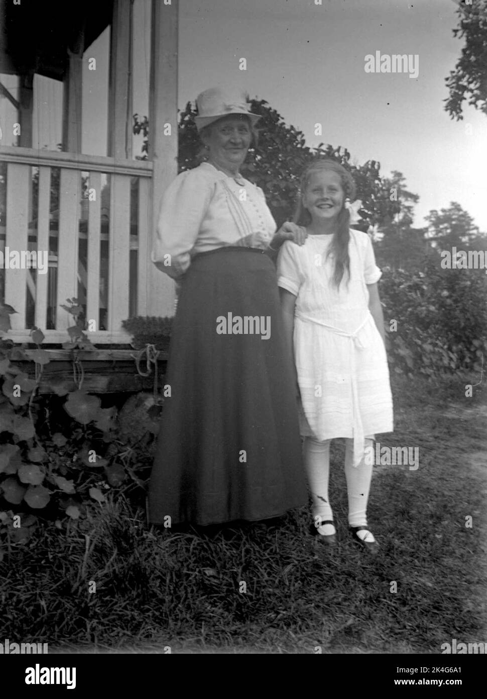 Full portrait of a woman and a girl below a porch. To the left, the ...