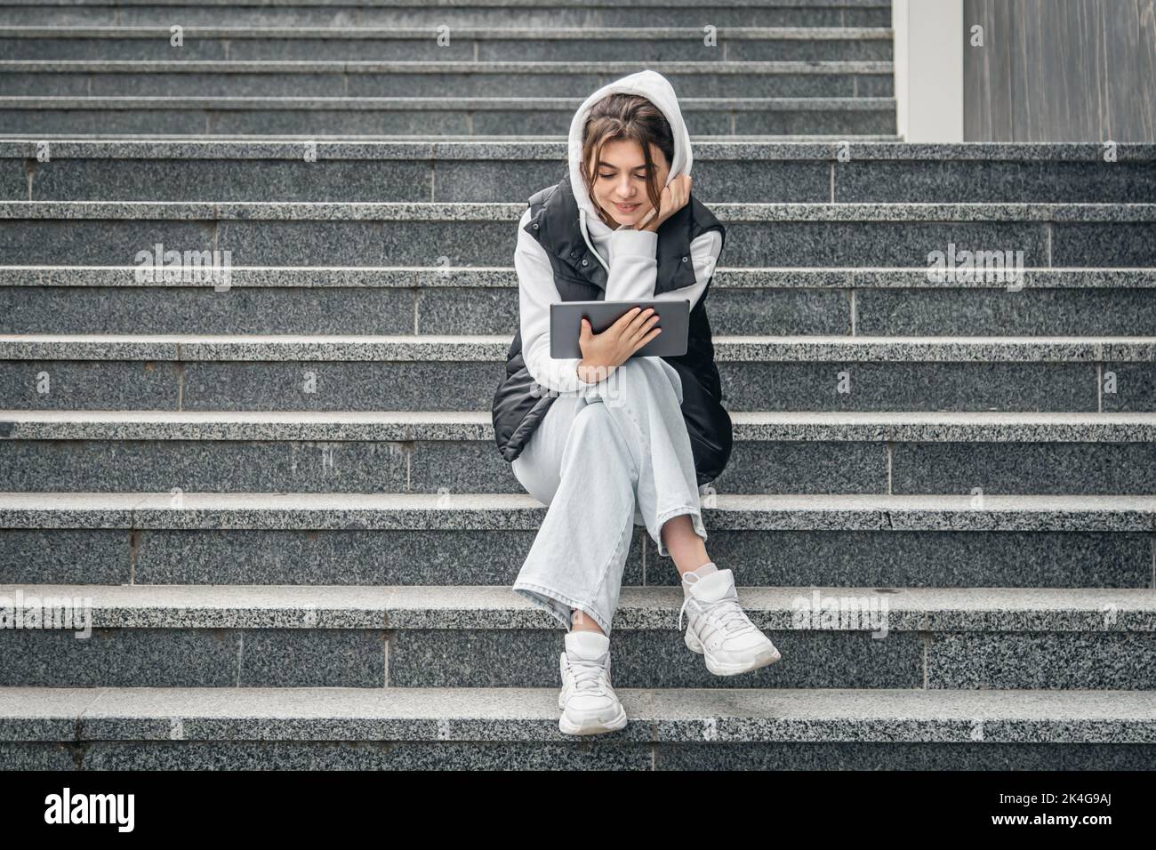 A young female student stands with a digital tablet in her hands ...