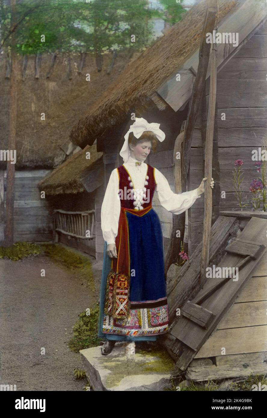 Woman in folk costume stands at a well at a lying house. Dressed in ...