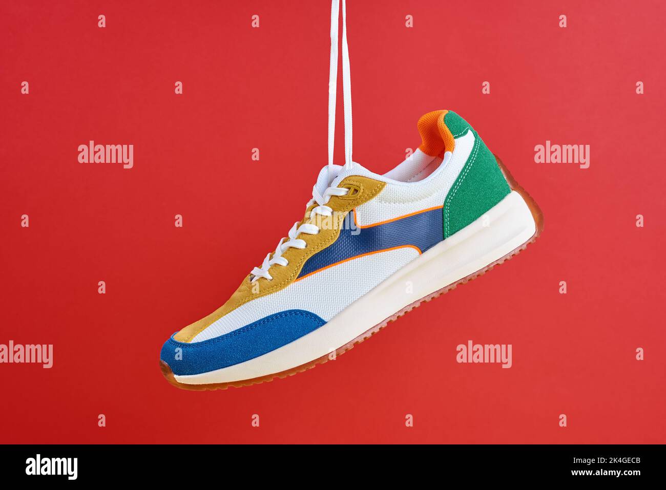 Hanging fashionable sneakers on red background. Stylish sports casual ...