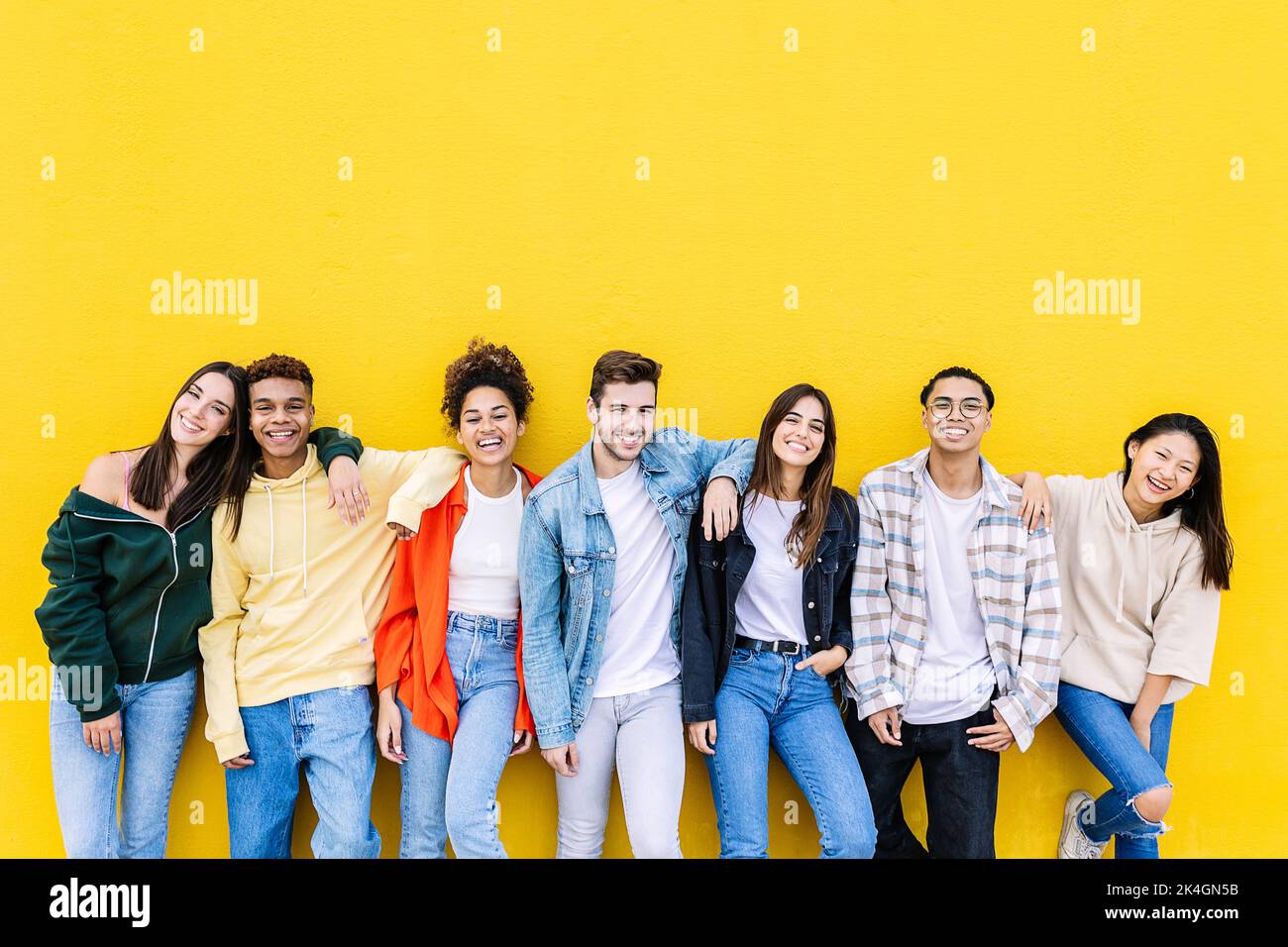 Smiling young group of multiracial happy friends leaning on yellow wall Stock Photo - Alamy