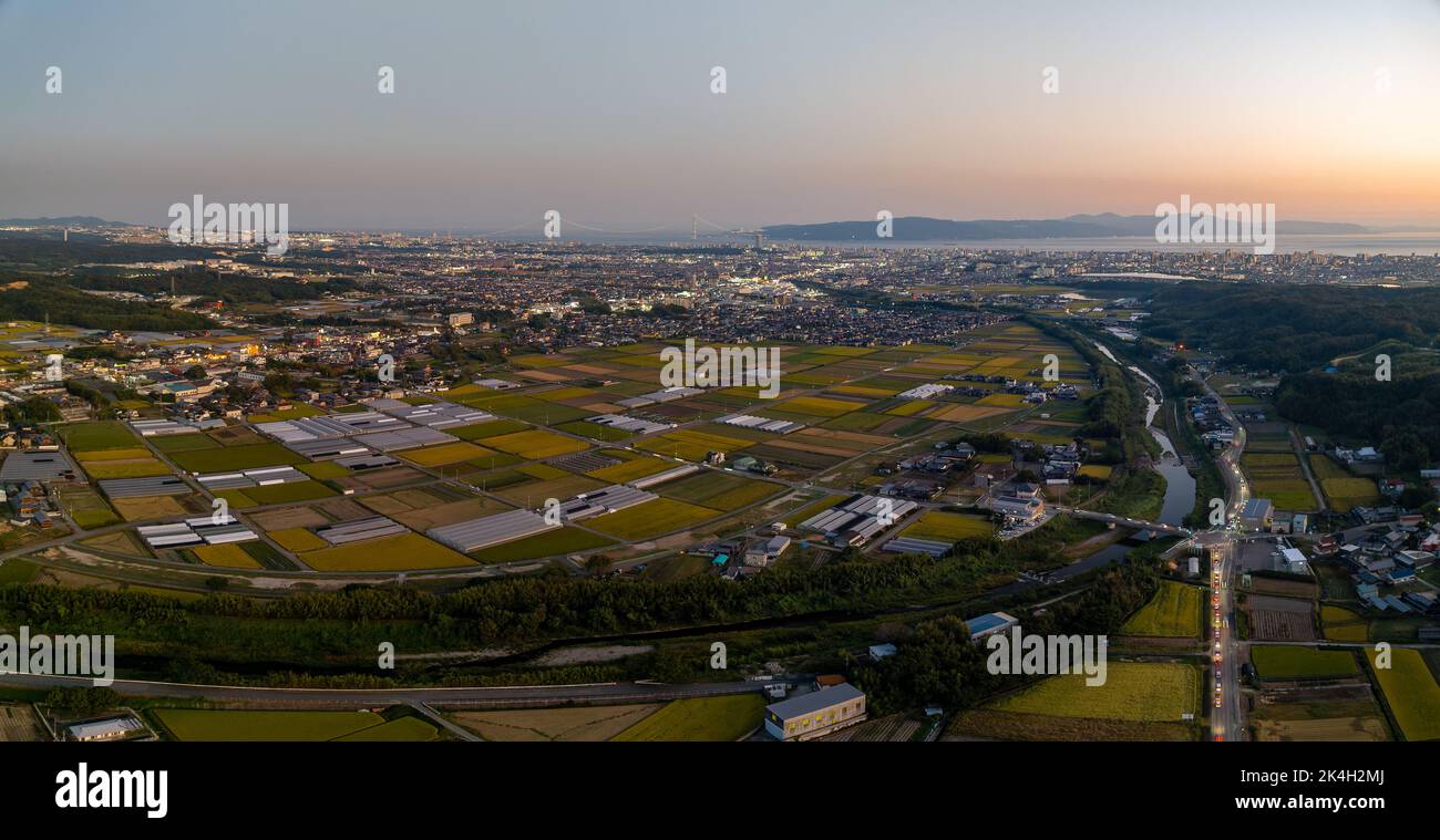Panoramic aerial view of coastal farms and lights from city at sunset ...
