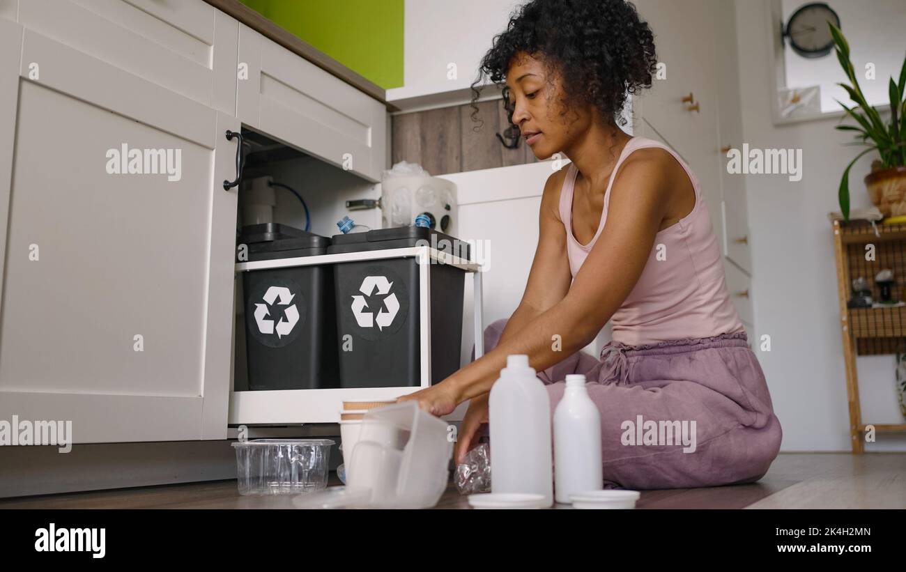 African American woman sits on floor sorting garbage. Young housewife ...