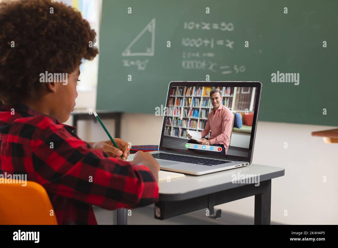 African american boy using laptop for video call, with smiling biracial male teacher on screen ...