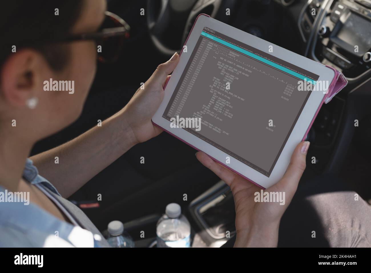 Biracial female programmer sitting in car, holding tablet with coding on screen. coding ...