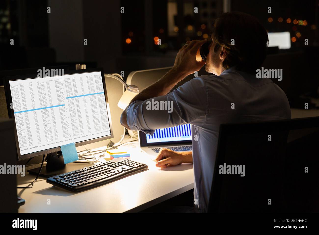 Caucasian Male Programmer Sitting At Desk Drinking Coffee Using Computer With Coding On Screen