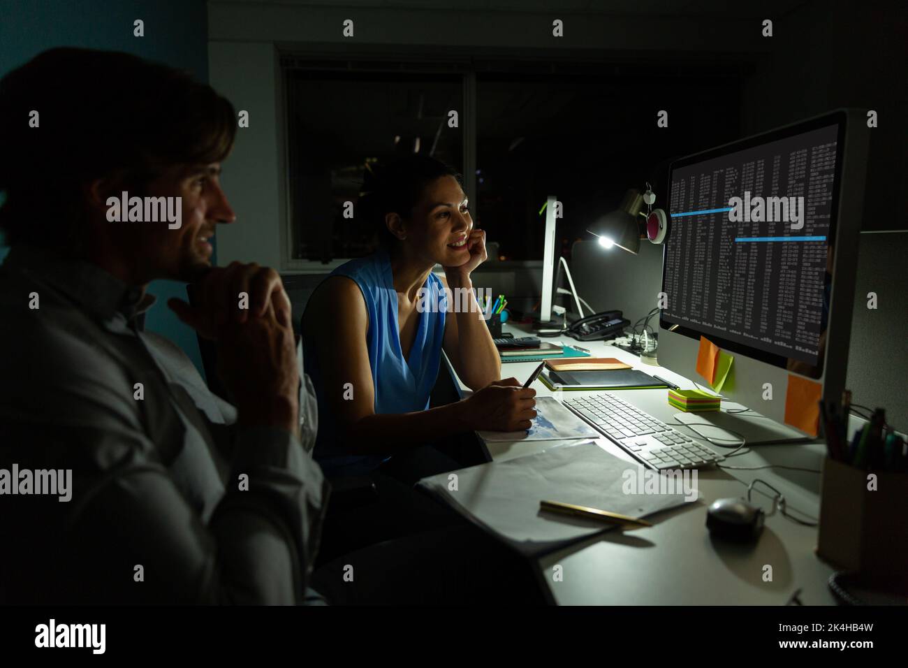 Two diverse male and female colleagues sitting at desk, using computer with coding on screen ...