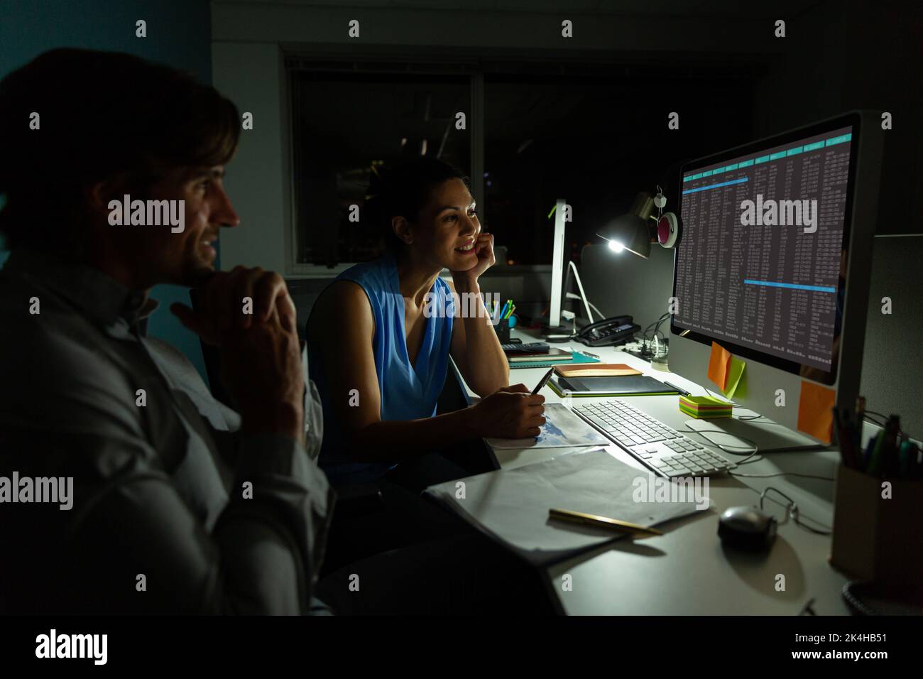 Two diverse male and female colleagues sitting at desk, using computer with coding on screen ...