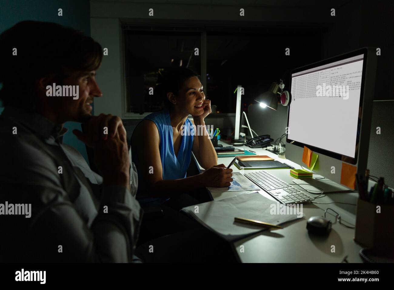 Two diverse male and female colleagues sitting at desk, using computer with coding on screen ...