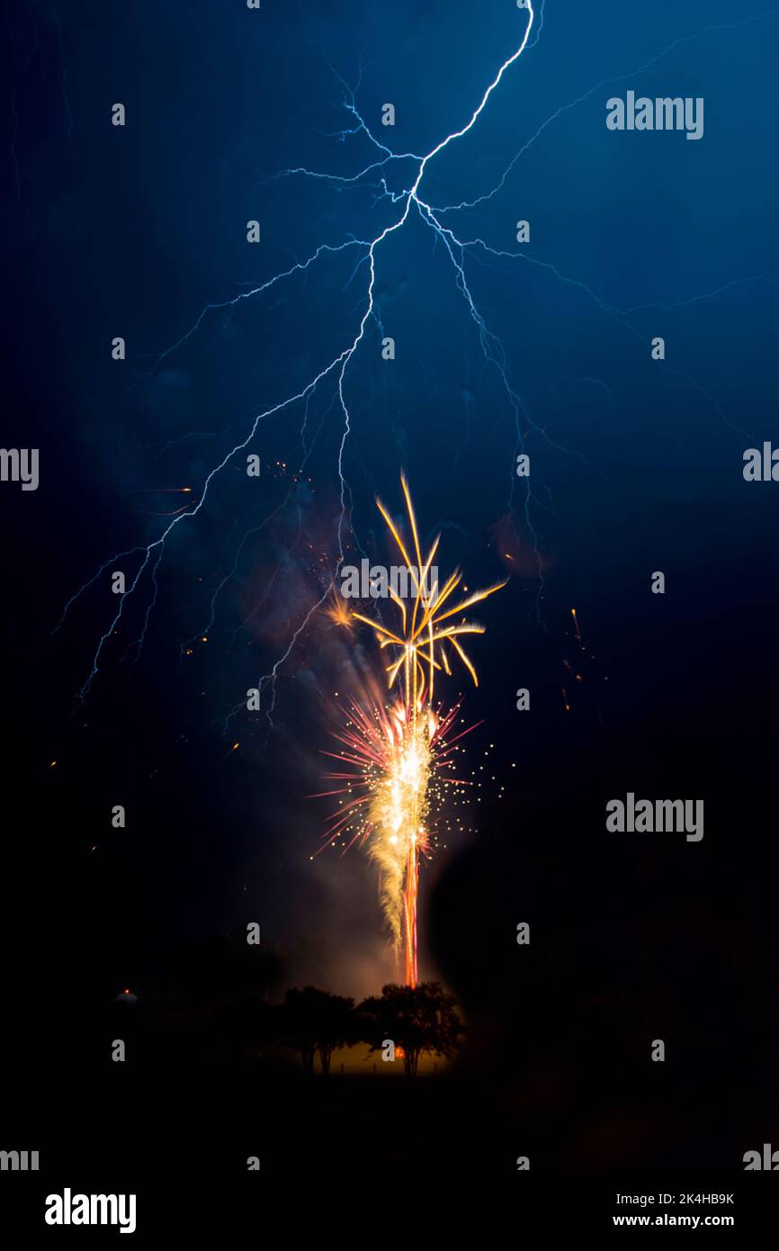 A vertical shot of fireworks exploding in a night sky while lightning ...
