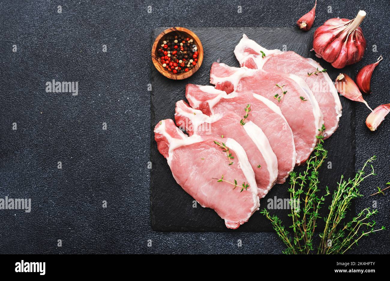 Raw pork chops, meat on slate board prepared for cooking with garlic ...