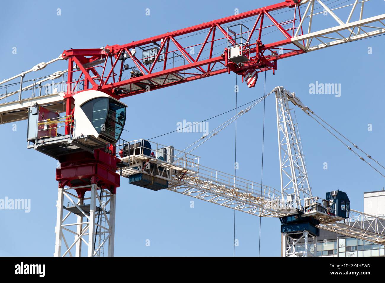 A close-up of two large, modern construction cranes, one red and one ...