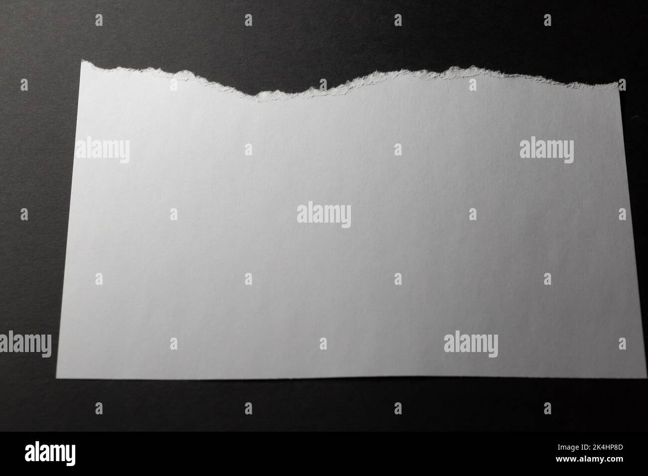 Horizontal sheet of white paper with torn top edge on black background ...