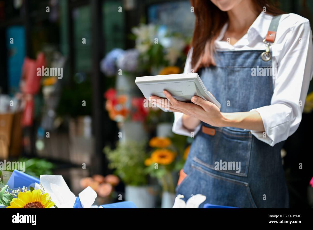 Attractive young Asian female florist or flower shop owner using ...