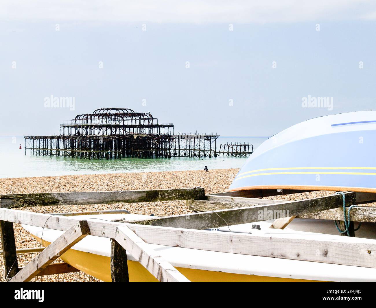 Dinghy on rack on beach and steel framework remains of of old Brighton ...