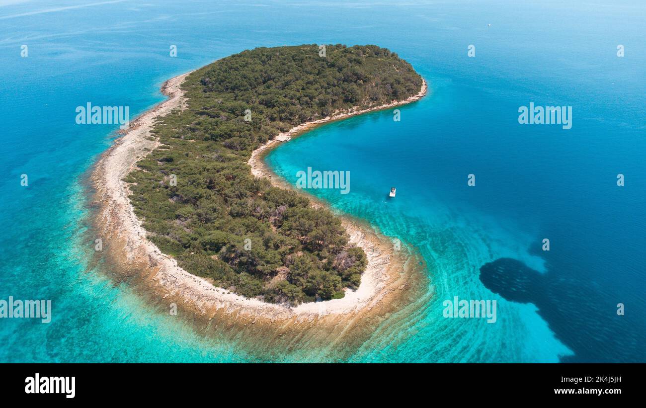 An aerial shot of an island with a boat on the blue water on a sunny ...