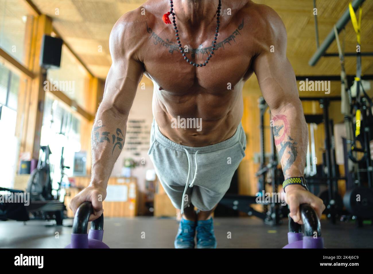 Cropped photo of a strong man doing push ups using kettlebells in a gym ...