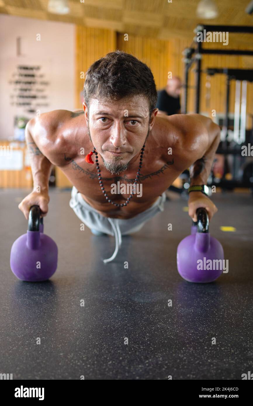 Vertical photo of a strong man doing push ups using kettlebells in a ...
