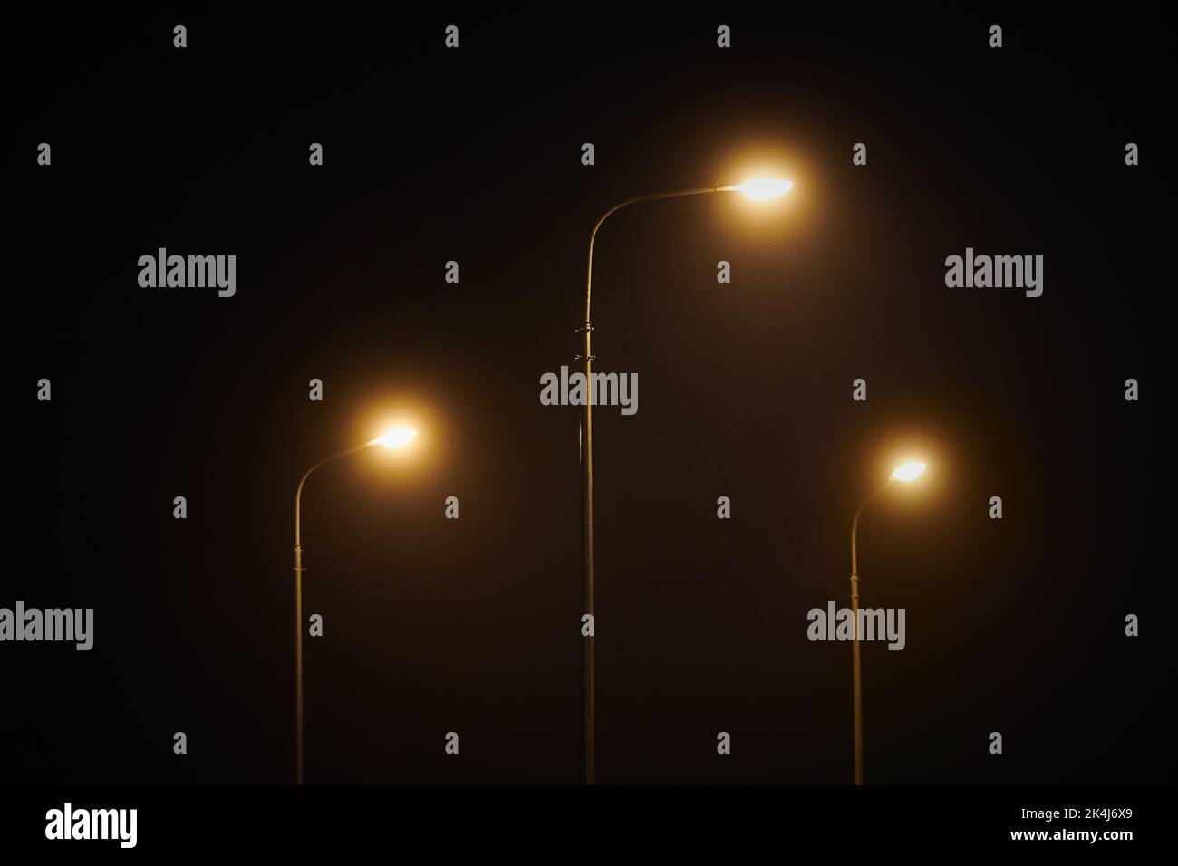 Three night lampposts shines with faint mysterious yellow light through ...