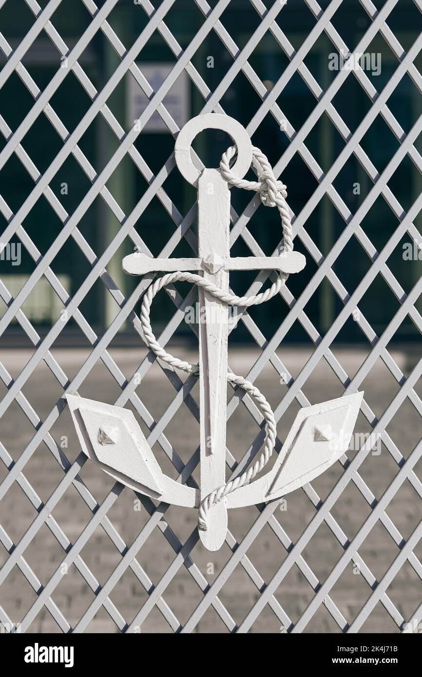 White anchor with mooring rope on mesh fence as symbol of navigation ...