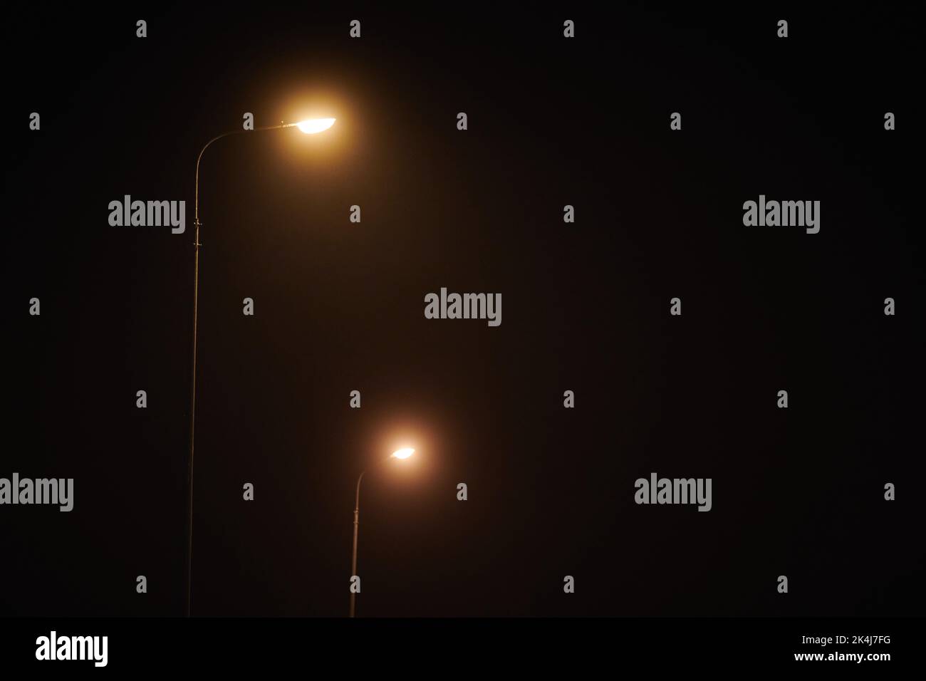 Two night lampposts shines with faint mysterious yellow light through ...
