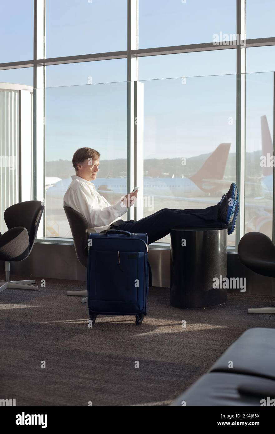 Caucasian businessman in fifties relaxing with legs up at airport ...