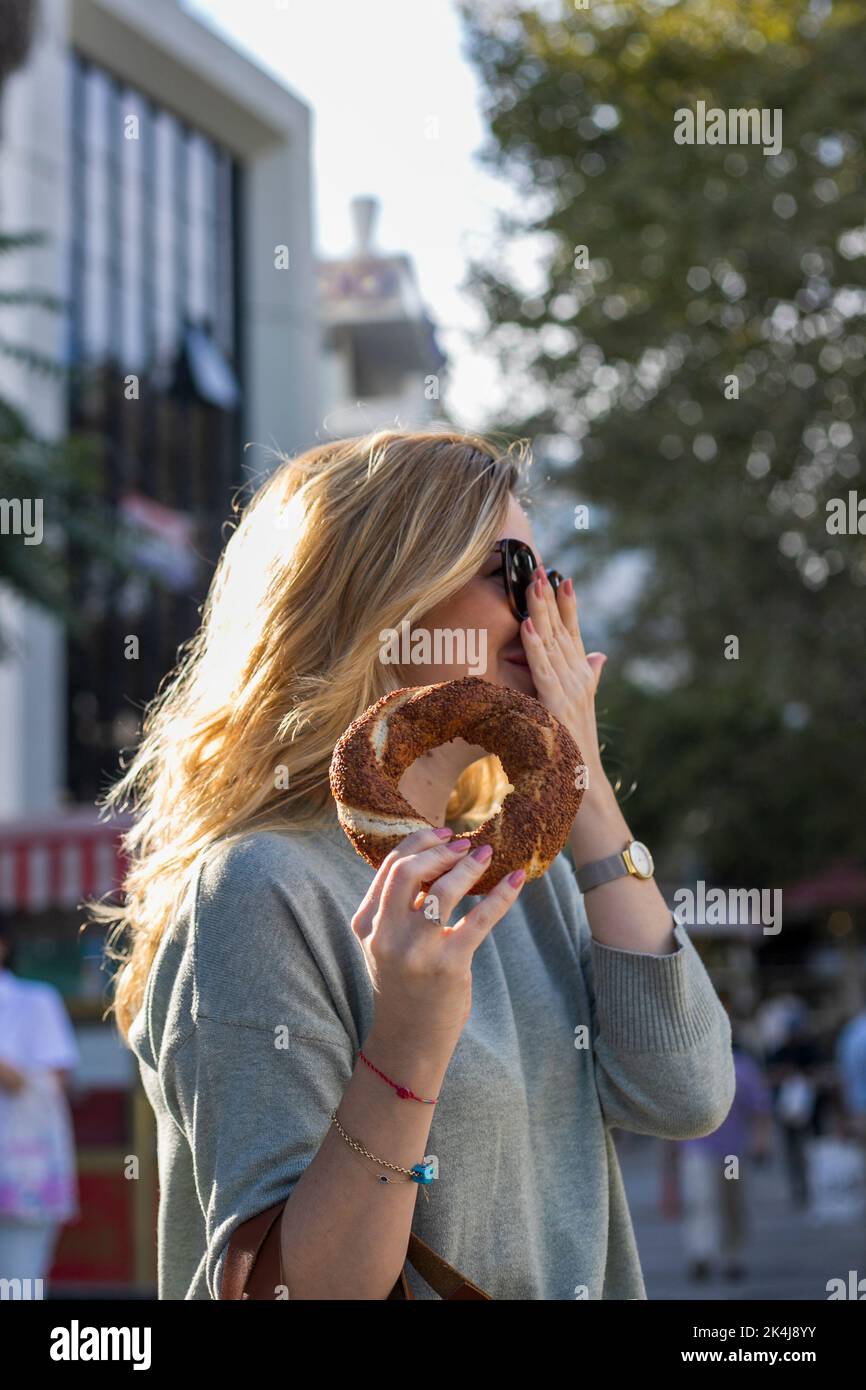 Blonde woman keep bagel on her hand and smiling. Street food, take away ...