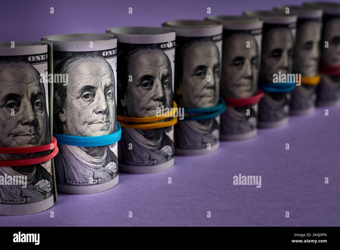 A row of rolled hundred dollar bills with rubber bands on purple ...