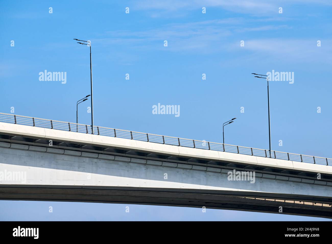 Concrete city bridge over river with street lampposts, blue sky ...
